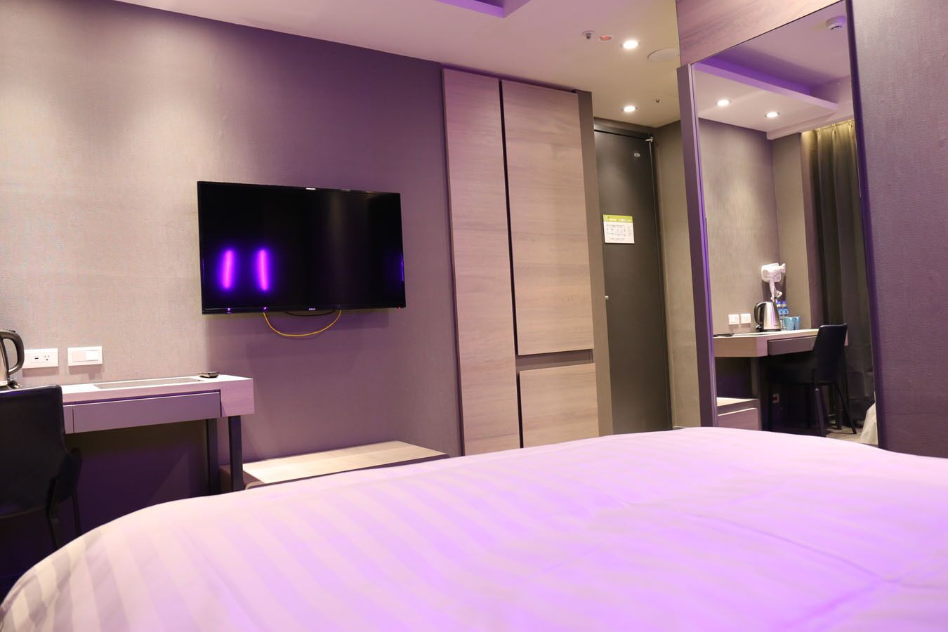 Quarto de hotel moderno com uma cama grande, televisão de tela plana na parede, uma escrivaninha com cadeira e um espelho.