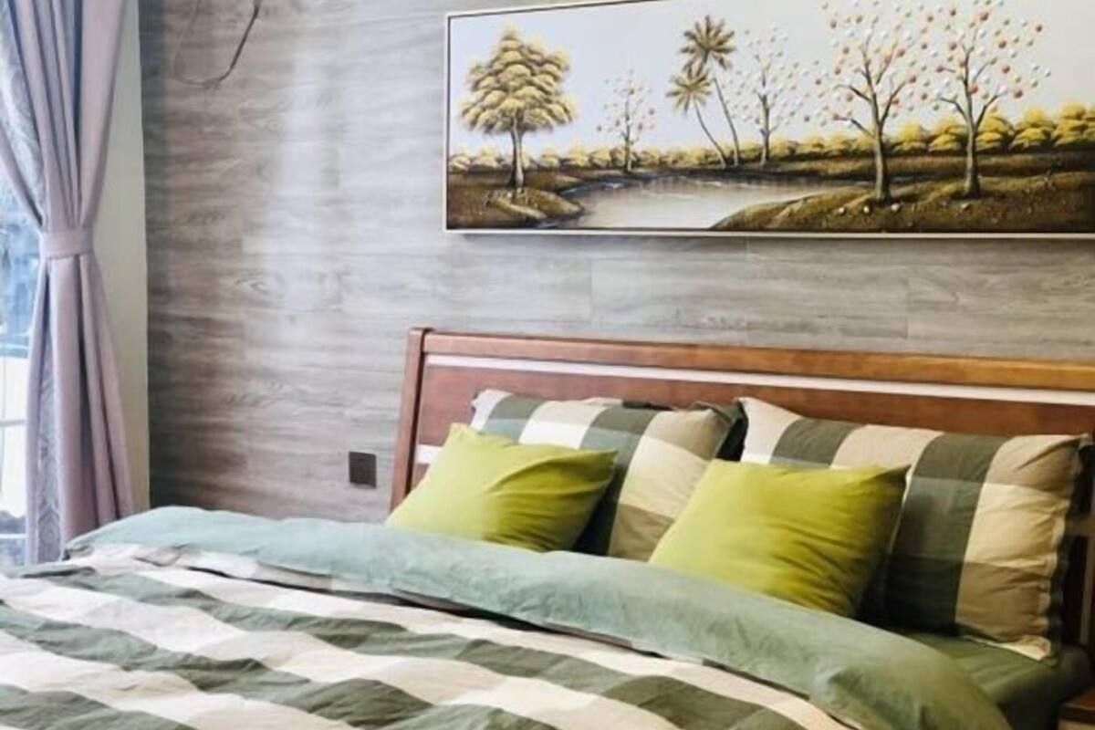 Quarto com cabeceira de madeira, cama com roupa de cama listrada e pintura de uma paisagem na parede.