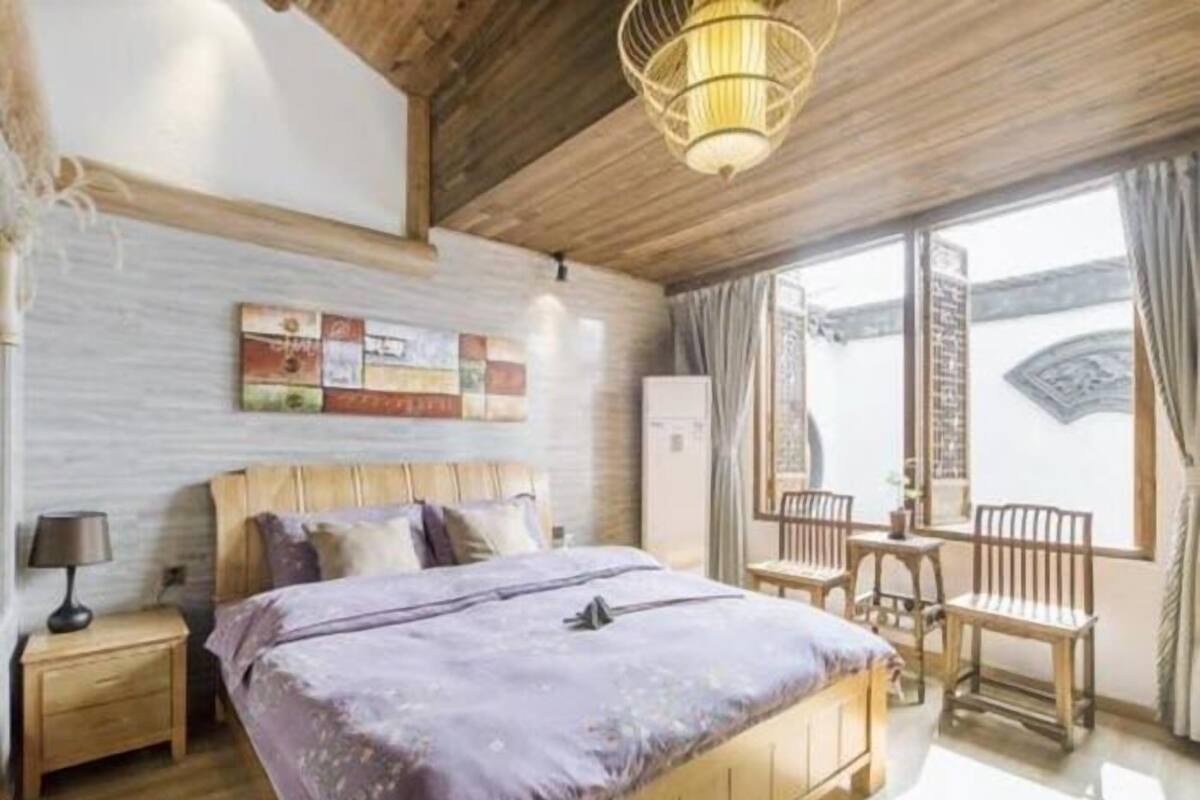Quarto com cama de madeira, mesa de cabeceira, luminária na parede e janela com cortinas.