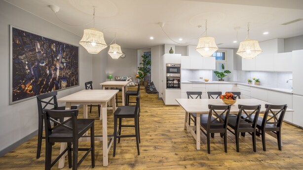 Uma cozinha moderna com armários brancos, uma área de jantar com mesas e cadeiras de madeira e luminárias pendentes.