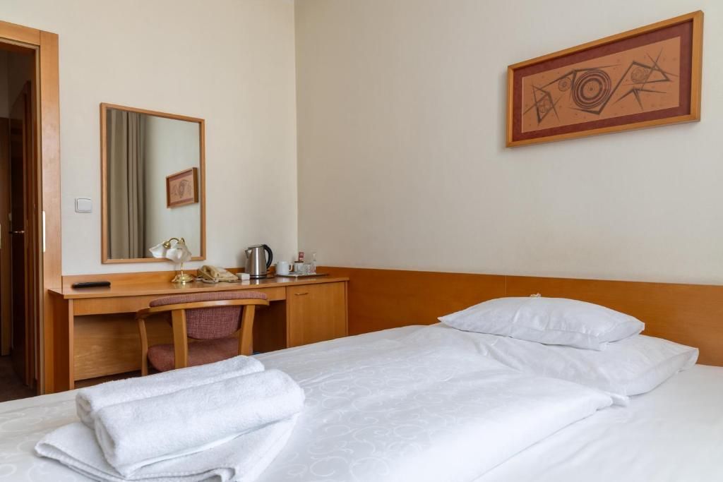Quarto de hotel com cama, escrivaninha, cadeira, espelho, obra de arte emoldurada e cafeteira.