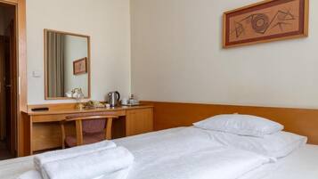 Quarto de hotel com cama, escrivaninha, cadeira, espelho, obra de arte emoldurada e cafeteira.