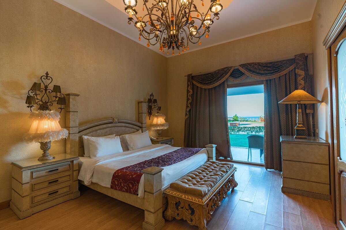 Quarto com uma cama grande, um banco, um lustre e vista para o exterior.