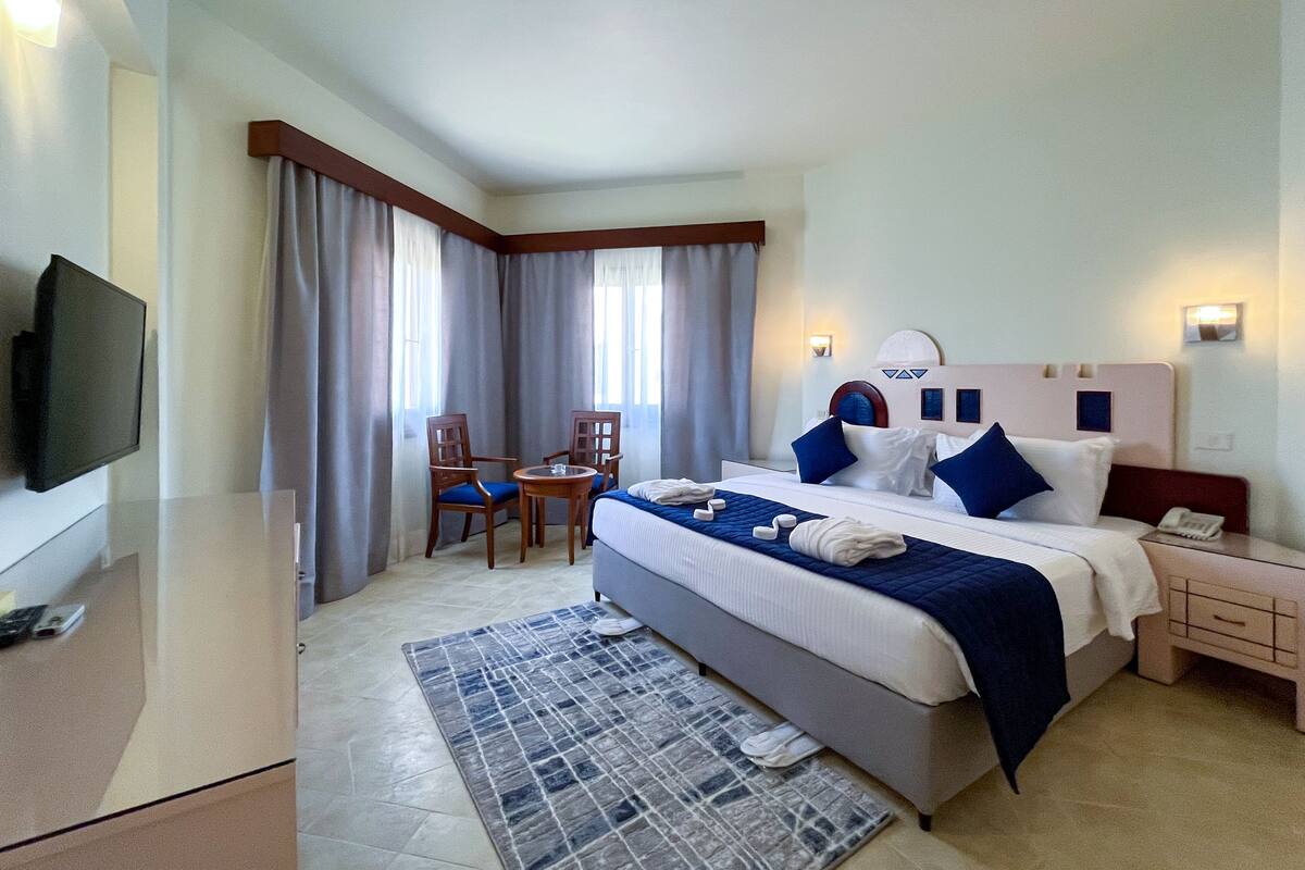 Quarto de hotel com cama, televisão, escrivaninha e cadeira.