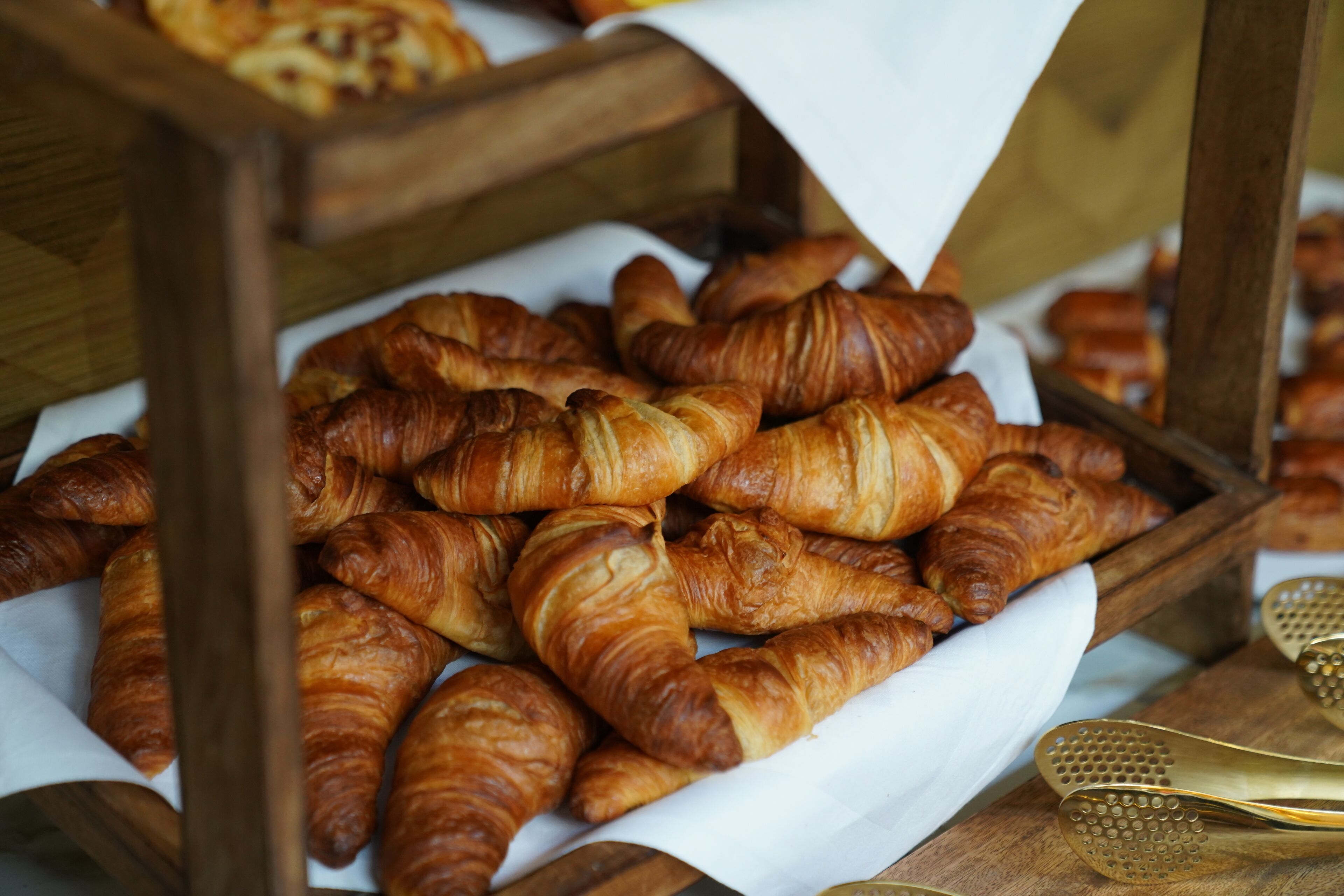 Uma bandeja de madeira com croissants sobre um tecido branco.