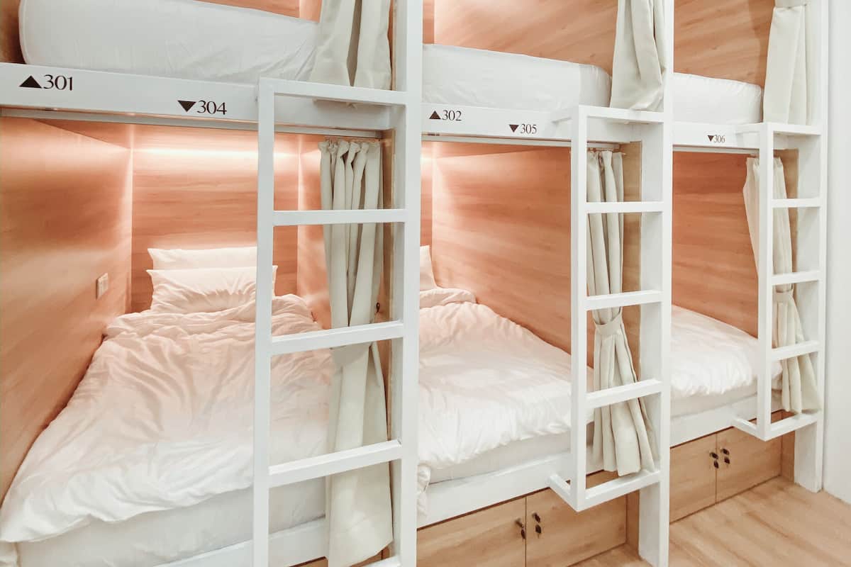 Quarto de hostel com beliches, paredes de madeira e cortinas.