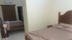 Um quarto com cama, mesa de cabeceira, ventilador e janela com cortinas.