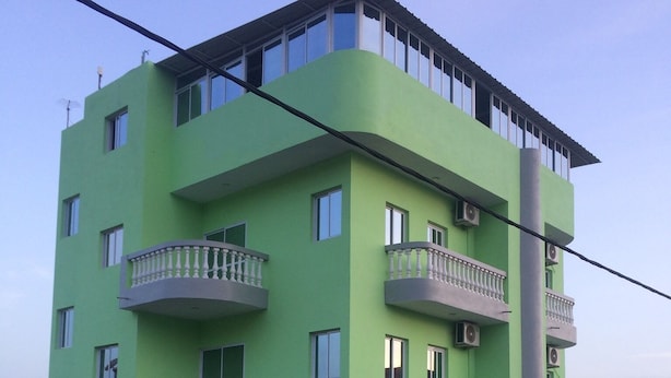 Um edifício com vários andares, varandas, uma placa indicando que é um hotel e uma área pavimentada.