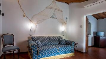 Quarto com sofá estampado, uma cadeira de madeira, ventilador de teto e televisão sobre um móvel.