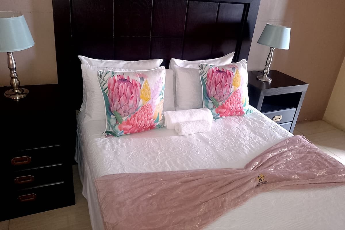 Cama bem arrumada com almofadas florais, cabeceira escura e mesas de cabeceira com abajures.