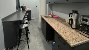 Uma cozinha moderna com bancada comprida, banquetas, máquina de café e geladeira.