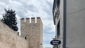 Uma rua com um muro de pedra e uma estrutura semelhante a um castelo ao fundo. Um letreiro do Hotel Seaway é visível à direita.