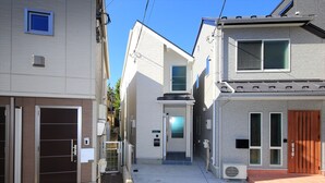 Uma rua estreita urbana com edifícios residenciais, incluindo uma porta de garagem, uma pequena janela e uma porta com uma placa que diz "otaka".