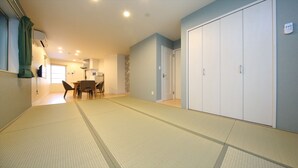 Um quarto amplo com piso de tatame, área de refeições com mesa e cadeiras, e guarda-roupa com portas deslizantes.