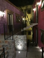 Uma passagem estreita com uma escadaria de pedra que leva a um edifício com fachada rosa e uma varanda.