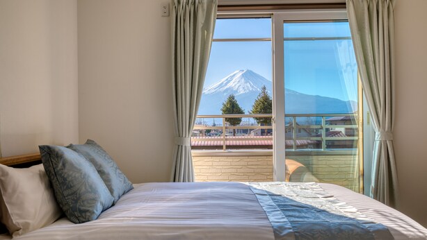 Quarto com cama, almofadas e vista para uma montanha pela janela.
