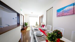 Uma sala de jantar de hotel com uma mesa comprida posta para quatro pessoas, cadeiras brancas e um jogo de toalha vermelho.