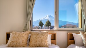 Quarto de hotel com duas camas, uma janela grande com vista para uma montanha e uma cortina.