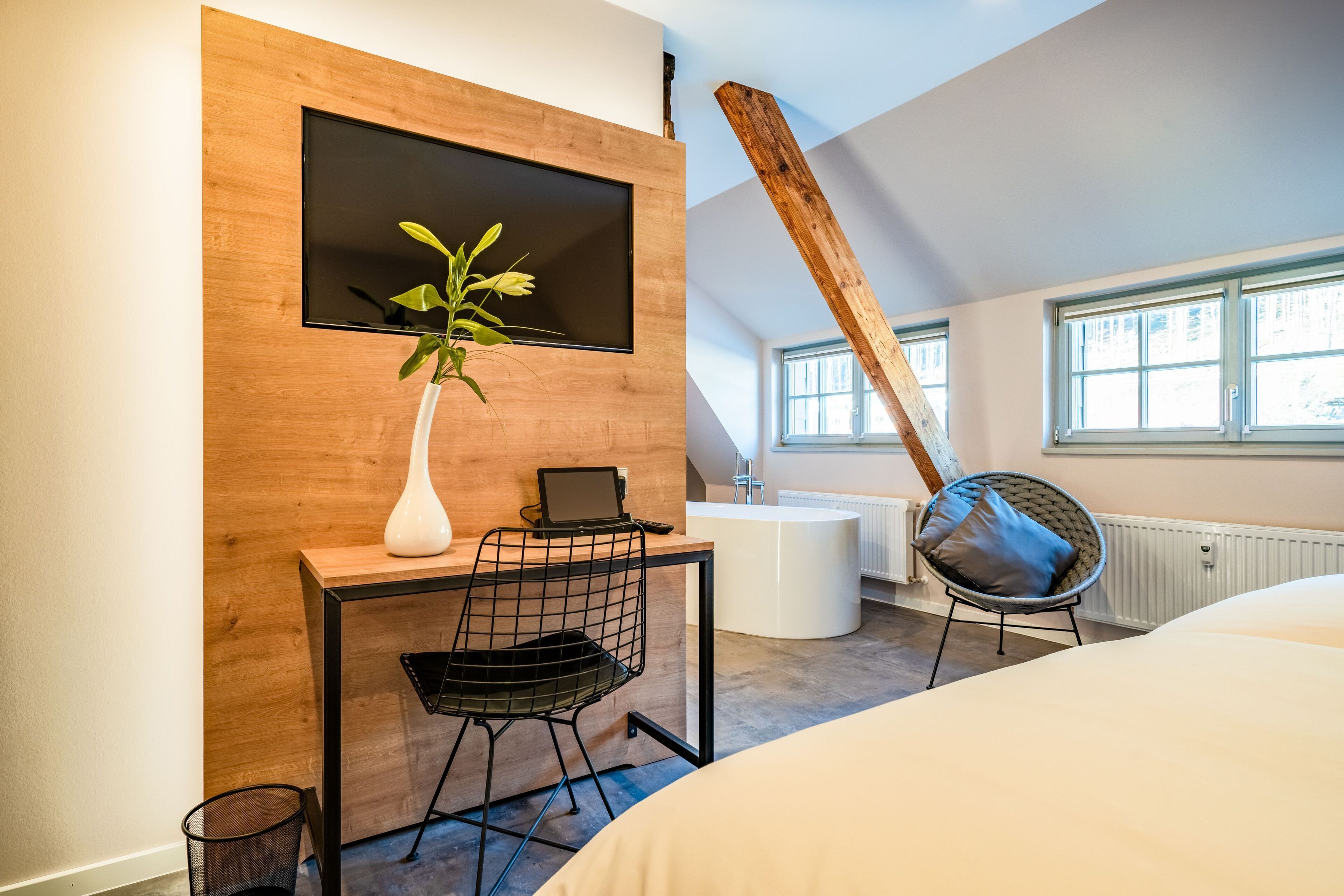 Quarto moderno com parede de destaque em madeira, televisão montada, escrivaninha com laptop, cadeira e cama.