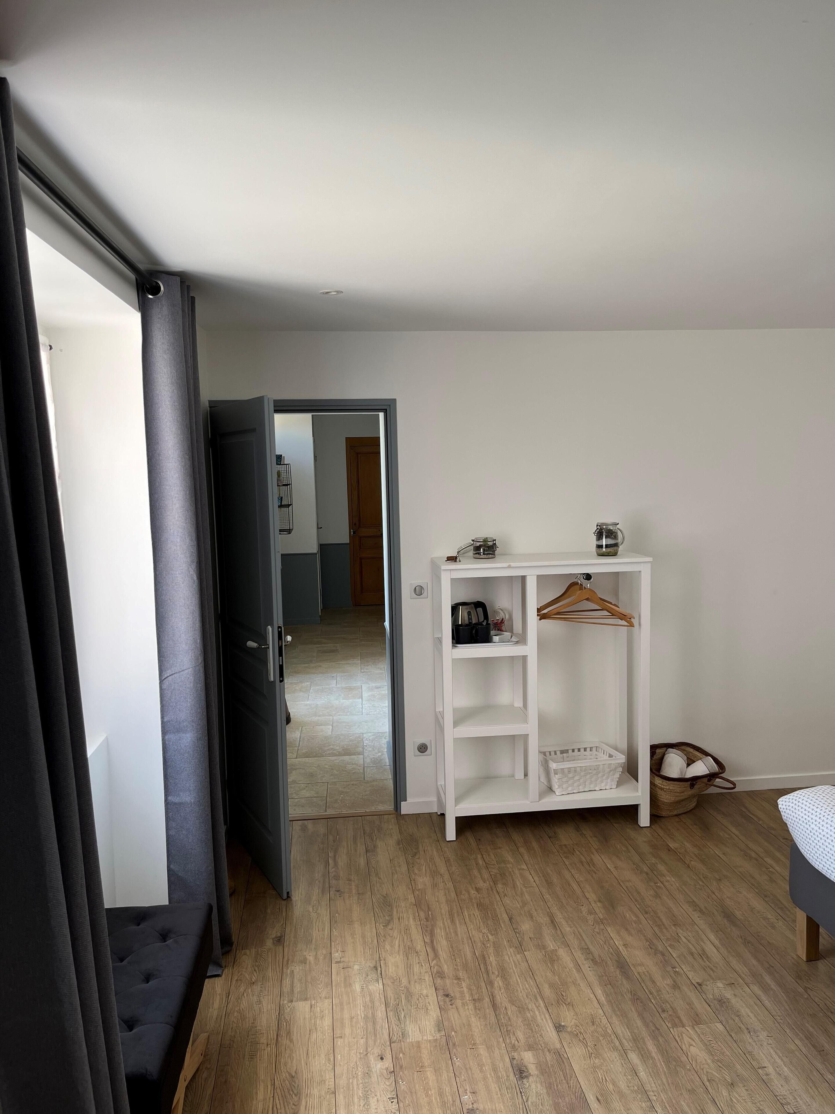 Quarto com piso de madeira, um guarda-roupa branco com prateleiras, uma mesa pequena e uma cesta.