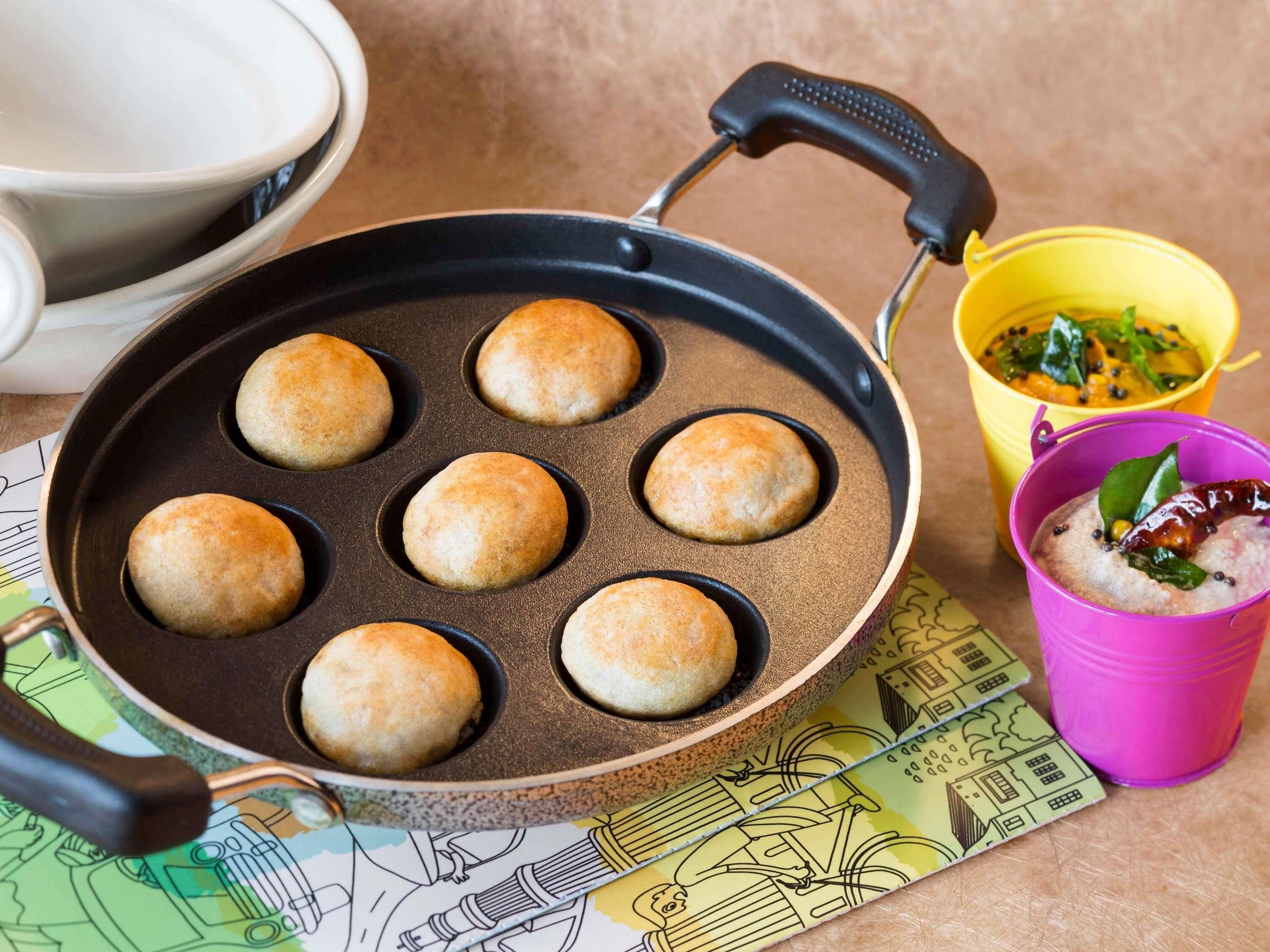 Uma panela com seis pães dourados e duas chávenas coloridas com comida.