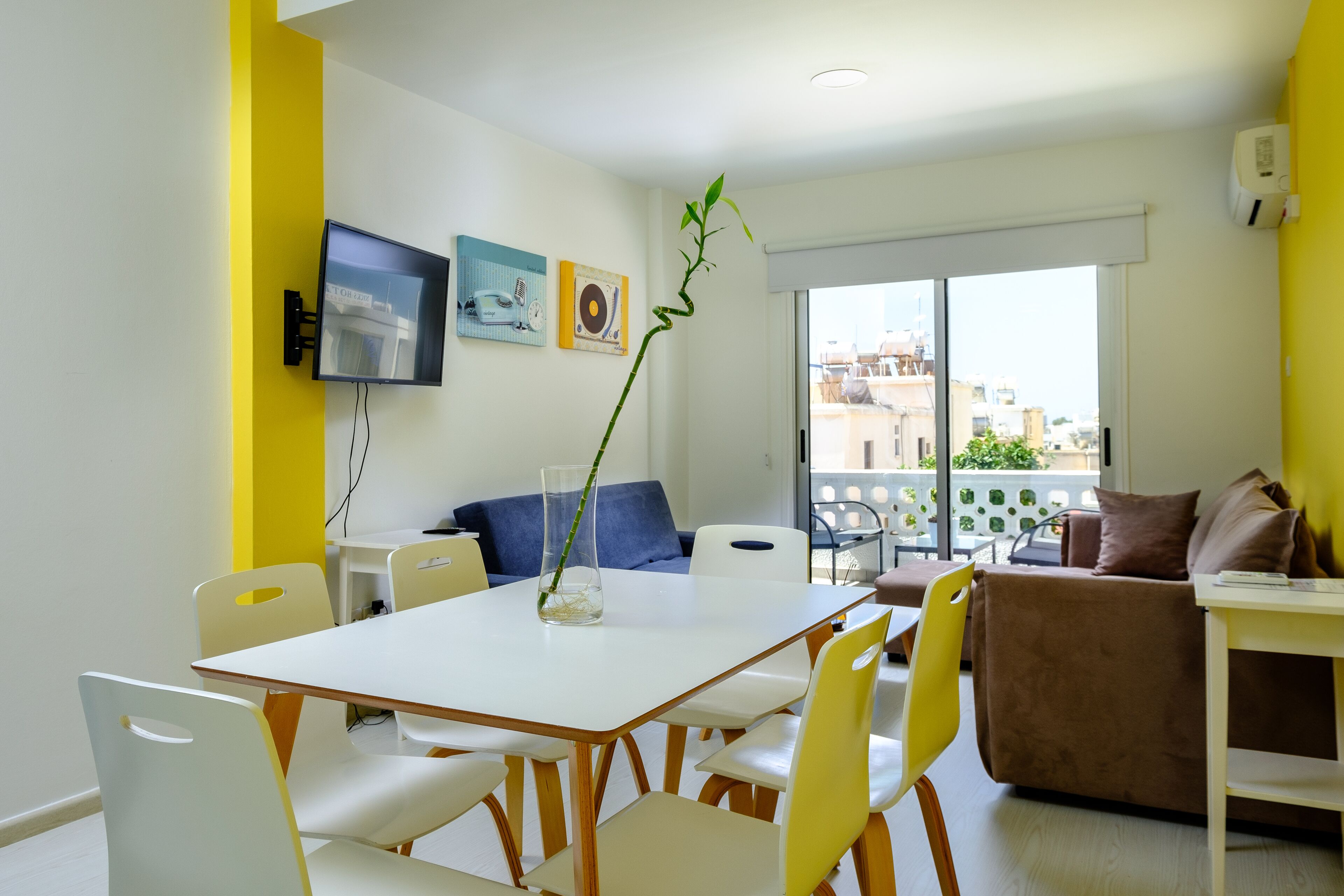 Uma sala de estar moderna com área de jantar, apresentando televisão de tela plana, obras de arte e uma grande janela com vista para a cidade.