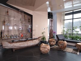 Um interior moderno com uma grande embarcação de madeira como peça central, prateleiras de vidro transparente com diversos objetos e uma grande janela com vista para árvores cobertas de neve.