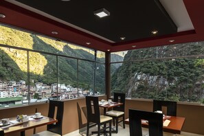 Uma área de refeições com vista para uma cidade montanhosa através de grandes janelas.