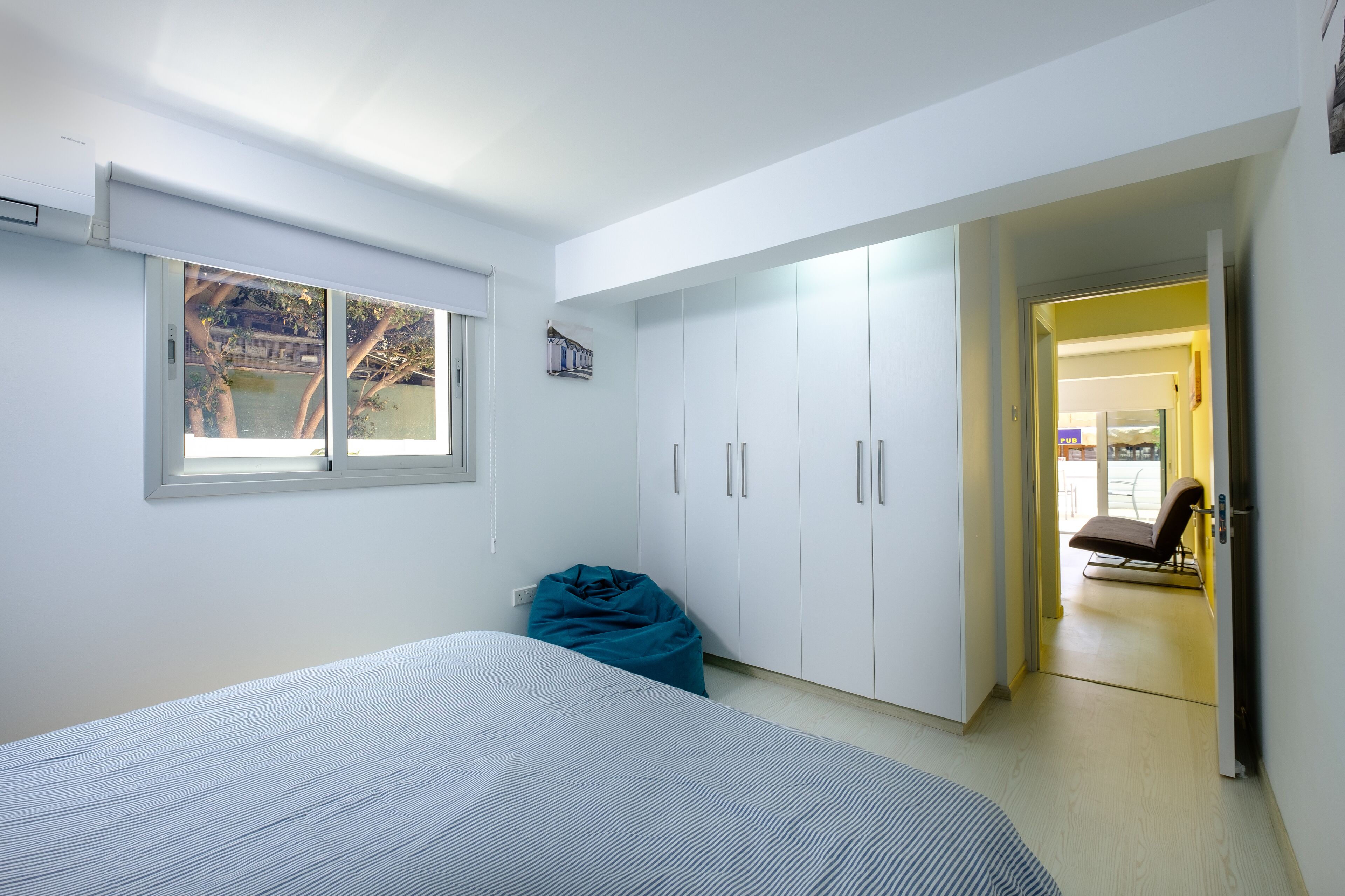 Quarto com cama, janela, guarda-roupa e um puff.