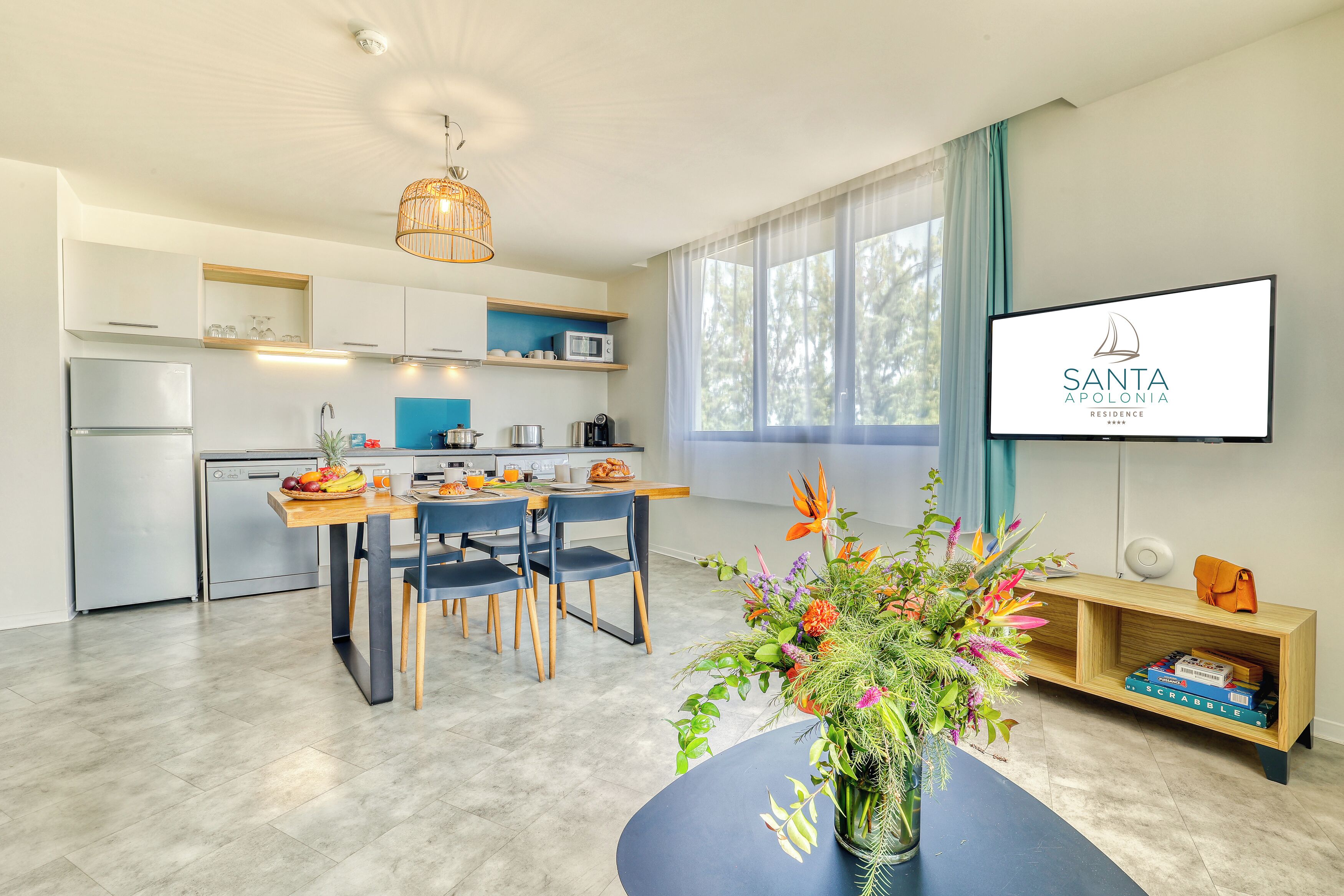 Cozinha moderna com área de refeições, uma TV exibindo 'SANTA APOLONIA RESIDENCE' e um arranjo de planta decorativa.