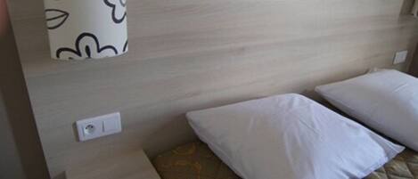 Quarto de hotel com cabeceira de madeira, mesa de cabeceira, duas almofadas e colcha estampada.