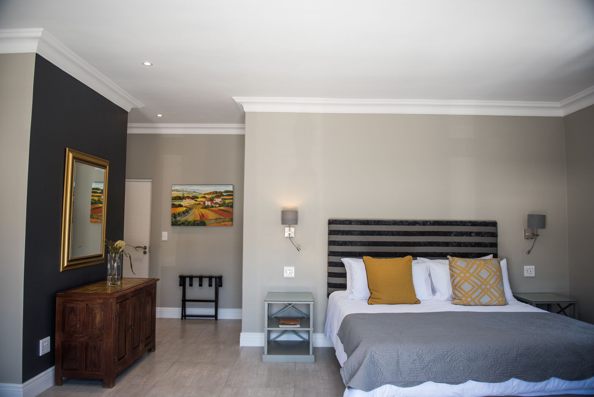 Quarto com cama, mesas de cabeceira, cômoda, espelho e um quadro na parede.