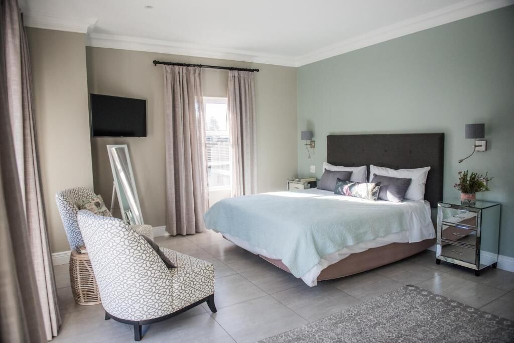 Quarto com cama grande, uma cadeira, televisão fixada na parede e mesa de cabeceira com abajur.