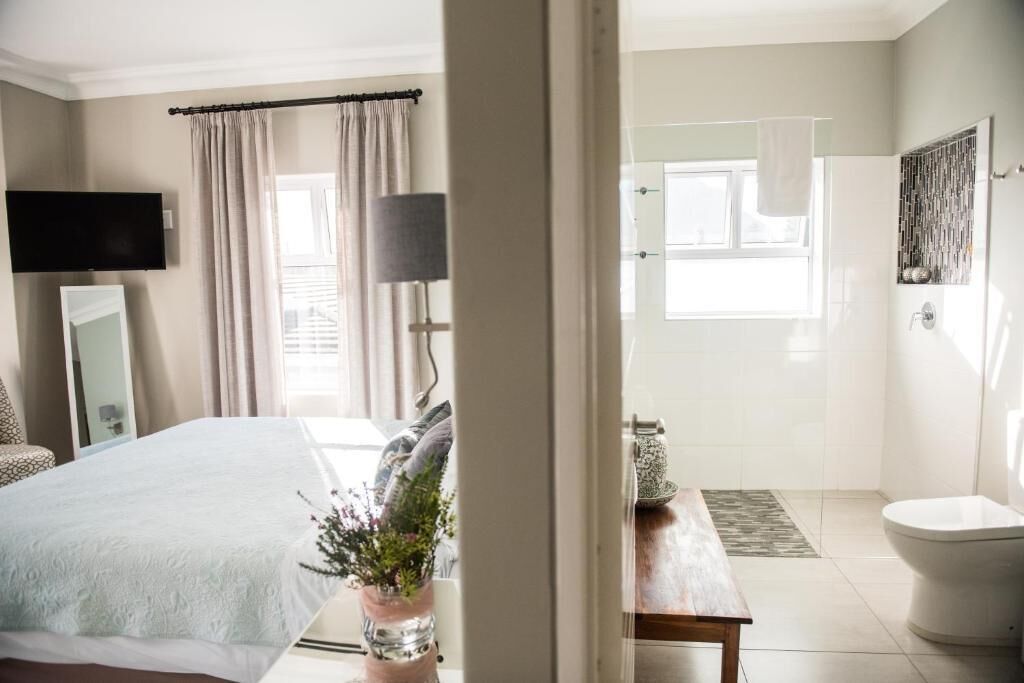 Quarto com cama, mesa de cabeceira, luminária, televisão e janela com cortinas.