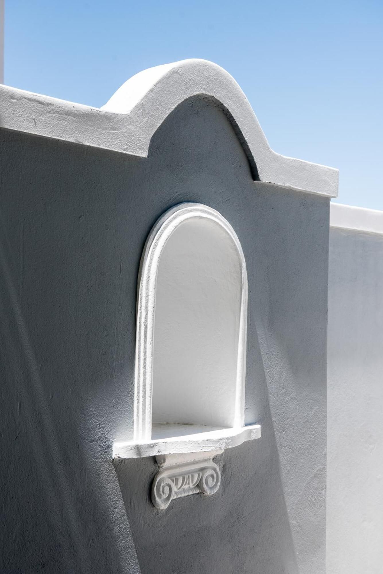Paredes brancas com um arco de metal decorativo e uma pequena janela.