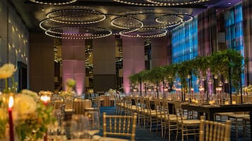 Uma sala de banquetes com mesas redondas, cadeiras e um pilar central.