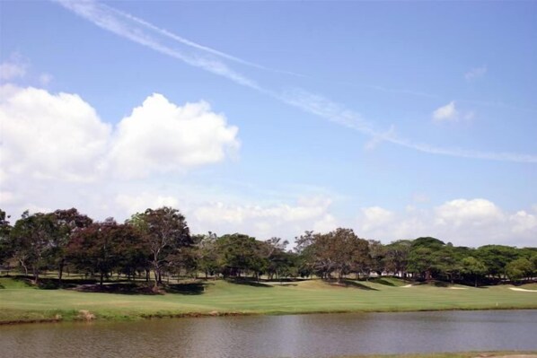 Um campo de golfe com lago, árvores e céu azul.