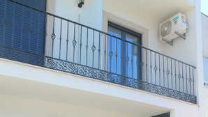 Uma mesa de piquenique de madeira com bancos, uma varanda com guarda-corpo decorativo e uma porta fechada.
