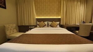 Quarto de hotel com uma cama grande, cabeceira com almofadas decorativas, uma escrivaninha com cadeira e cortinas.