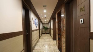 Corredor de hotel com piso de mármore, portas de madeira e um vaso de planta.