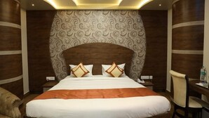Quarto de hotel com uma cama grande, duas mesas de cabeceira, uma cadeira e uma escrivaninha com cadeira.