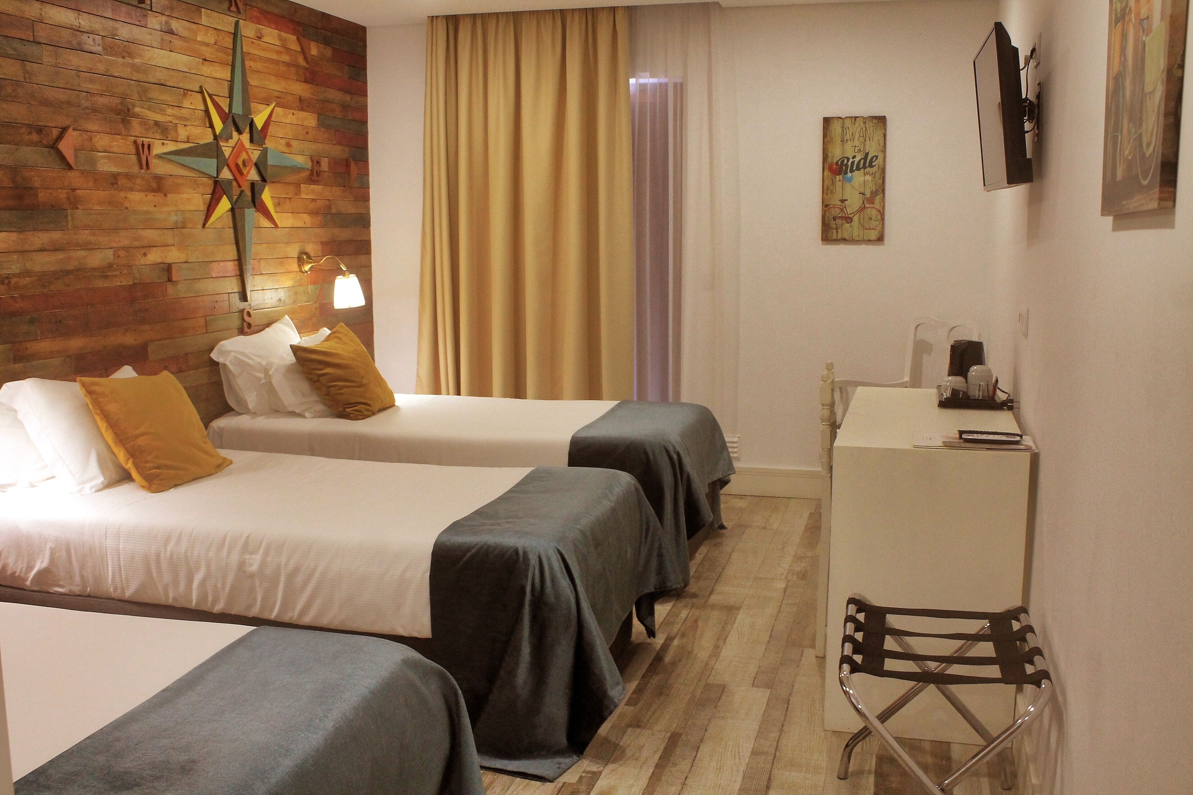 Quarto de hotel com duas camas, uma escrivaninha, uma cadeira, um abajur e um painel de parede com decoração de bússola.
