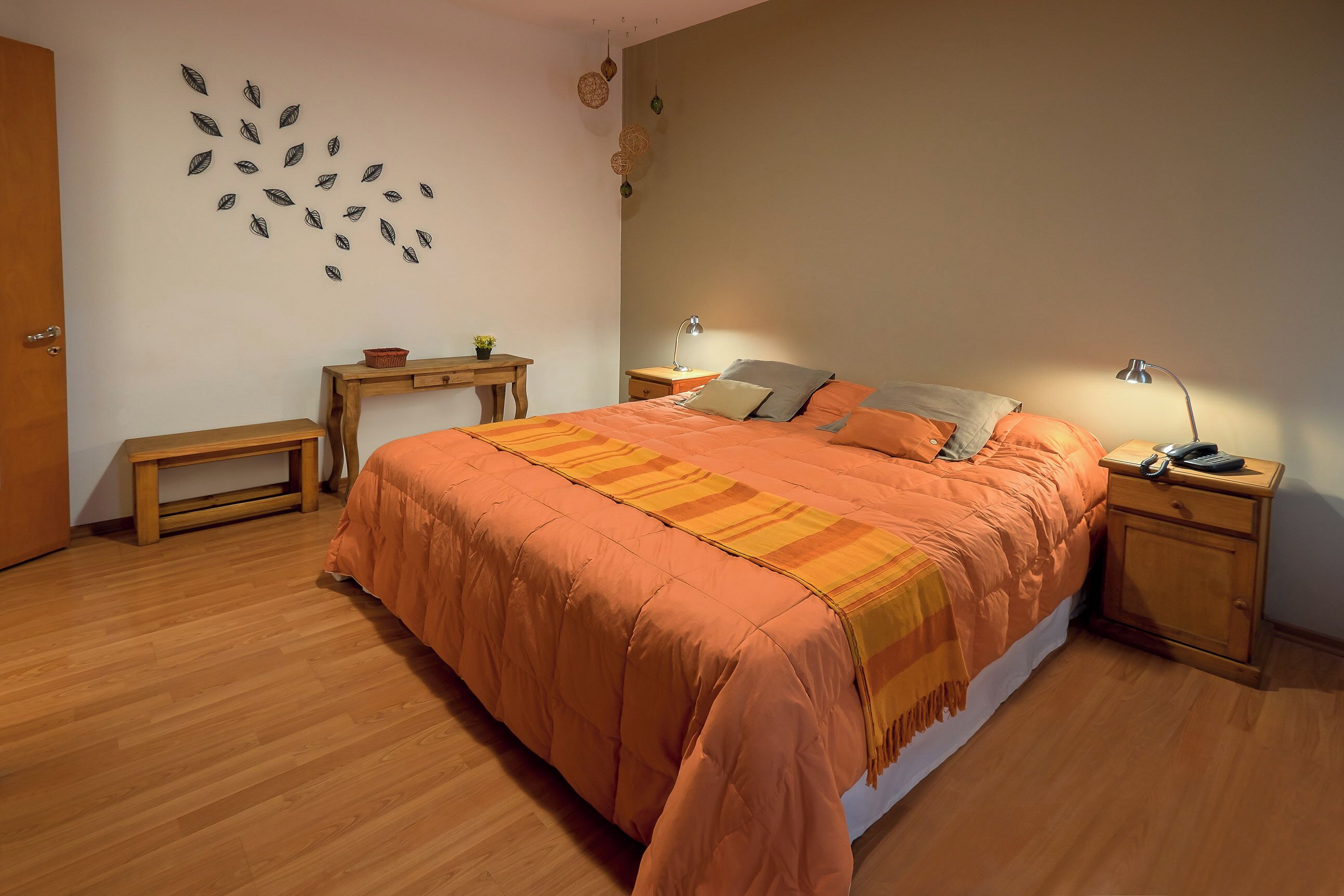 Quarto com cama grande, mobiliário de madeira, decoração na parede e mesa de cabeceira com abajur.