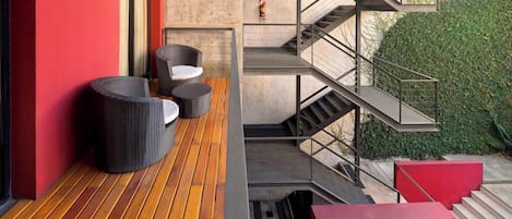 Uma área externa moderna com deck de madeira, um lance de escadas e uma parede vermelha.