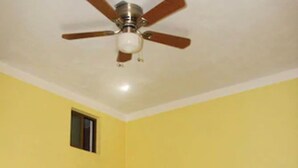 Quarto com duas camas de madeira, um ventilador de teto e uma janela pequena.
