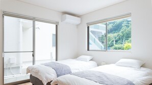 Quarto de hotel moderno com duas camas, janelas amplas e vista para o verde lá fora.