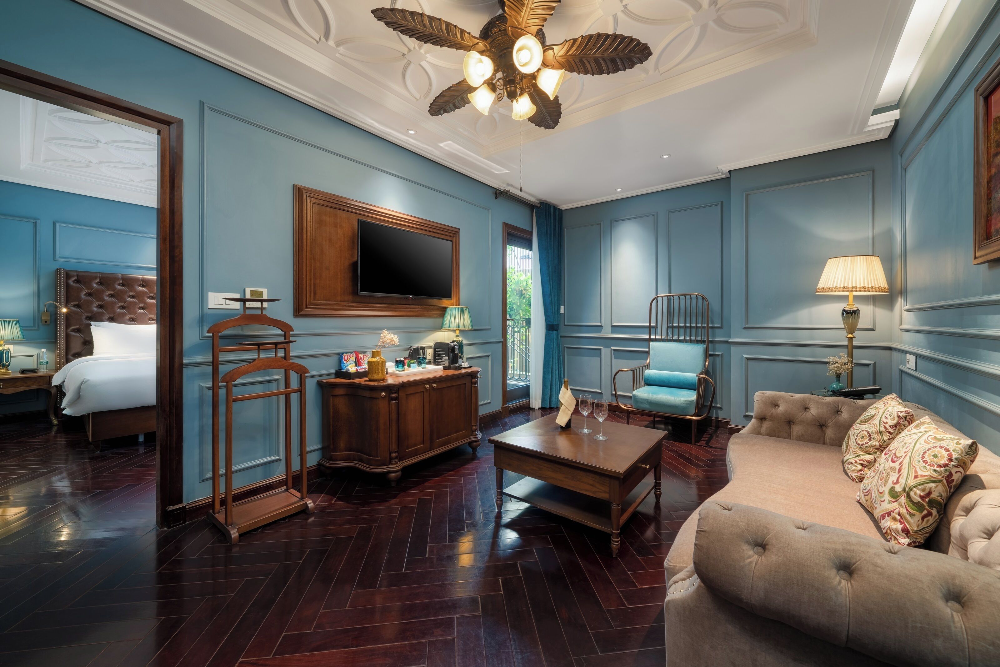 Quarto com uma cama grande, cômoda de madeira, televisão na parede, mesa de centro e sofá.