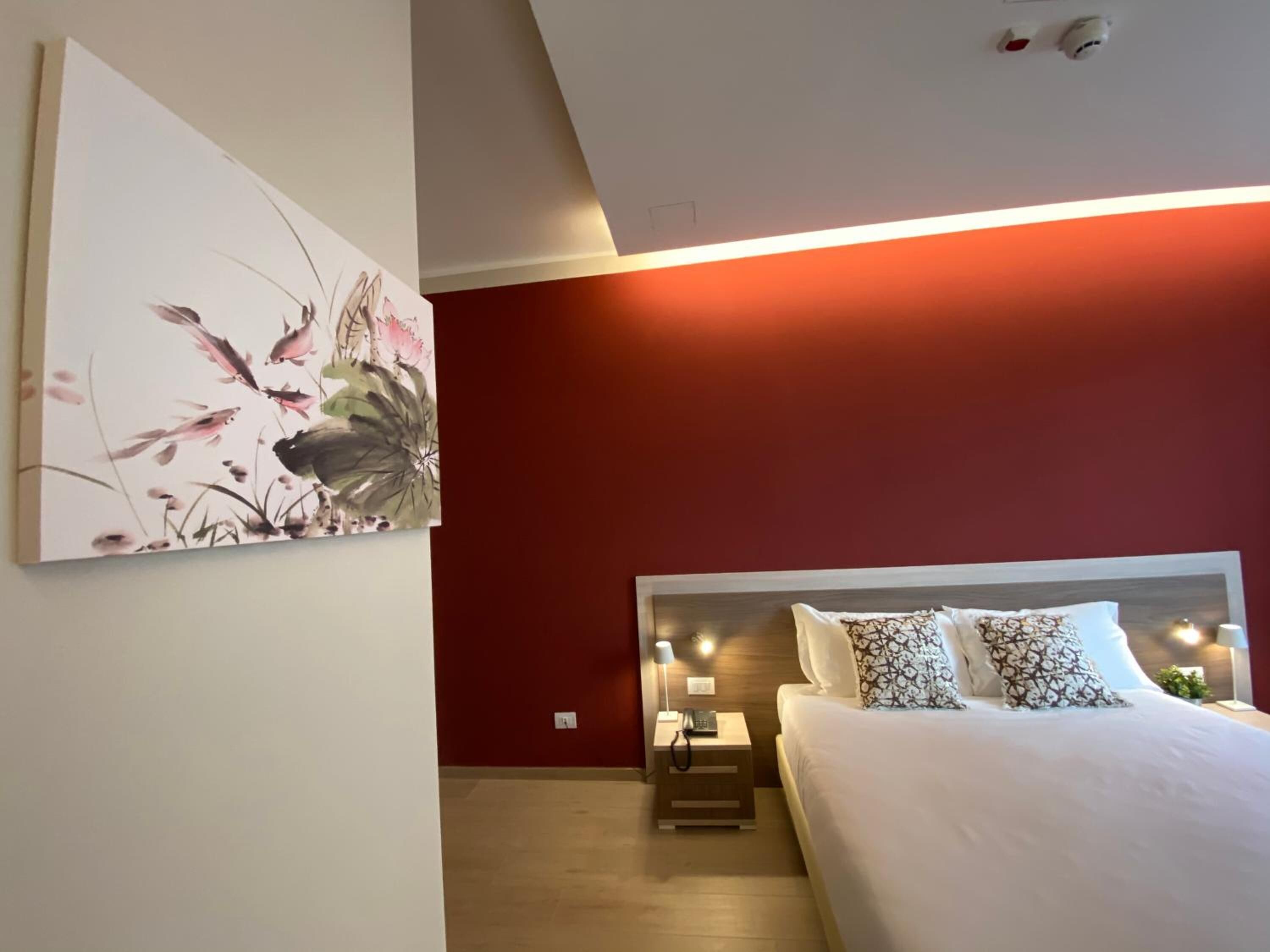 Quarto de hotel moderno com uma cama grande, uma mesa de cabeceira com abajur e uma câmera de segurança fixada na parede.