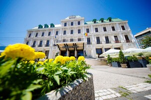 Um hotel imponente com fachada clássica, entrada destacada e um jardim bem cuidado com flores amarelas.