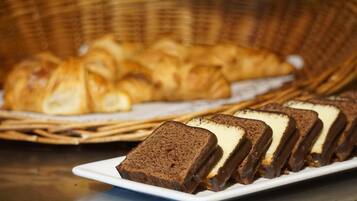 Uma fatia de bolo de chocolate com uma cesta de croissants ao fundo.